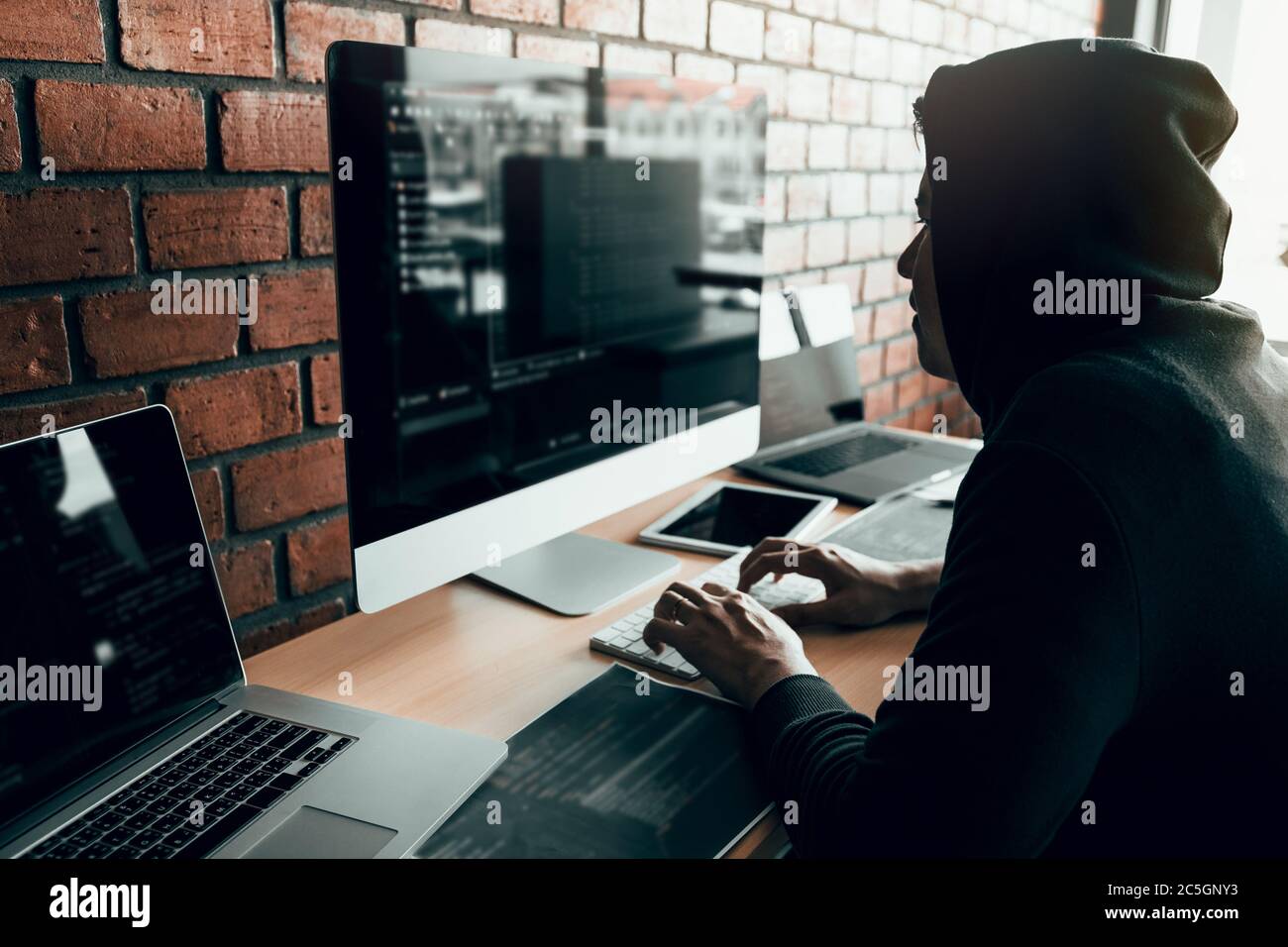 Hacker in the hood working with computer with hacking breaking into ...