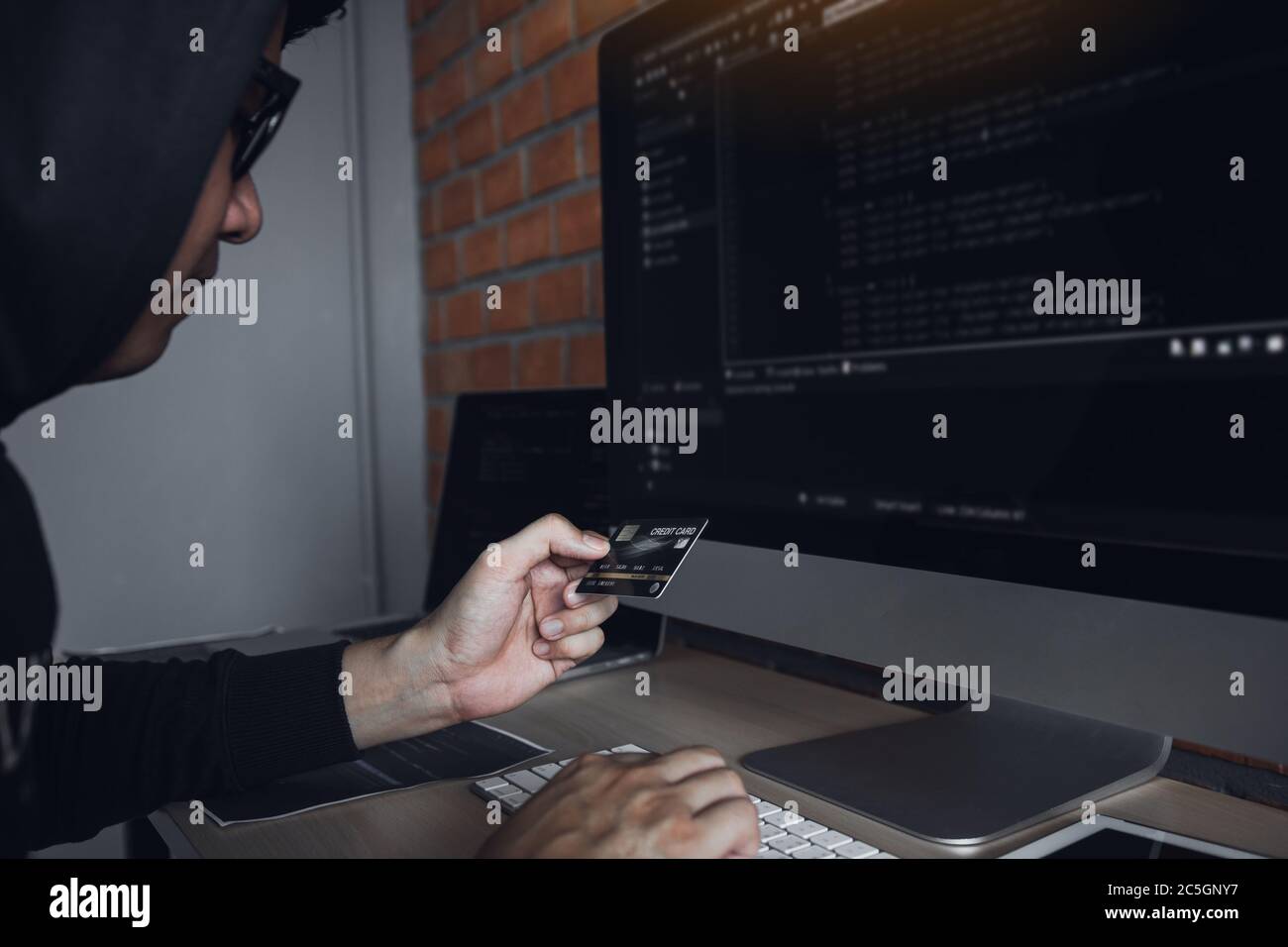 Hacker in the hood working with computer and holding credit card with ...