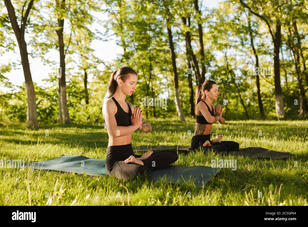 Two beautiful ladies in black sporty tops and leggings sitting in lotus ...