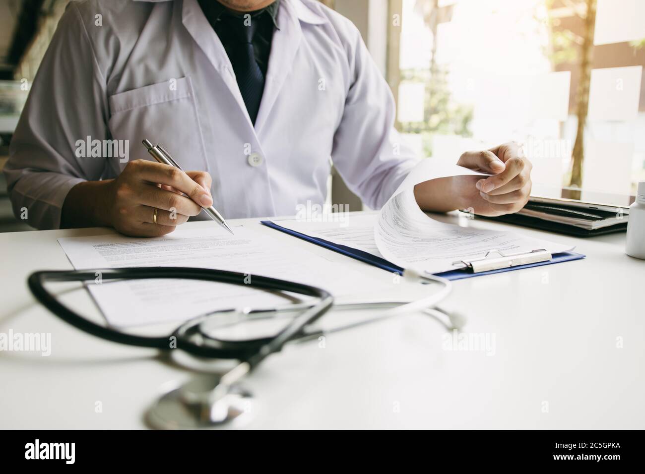 Doctor hand holding pen writing patient history list on note pad and ...