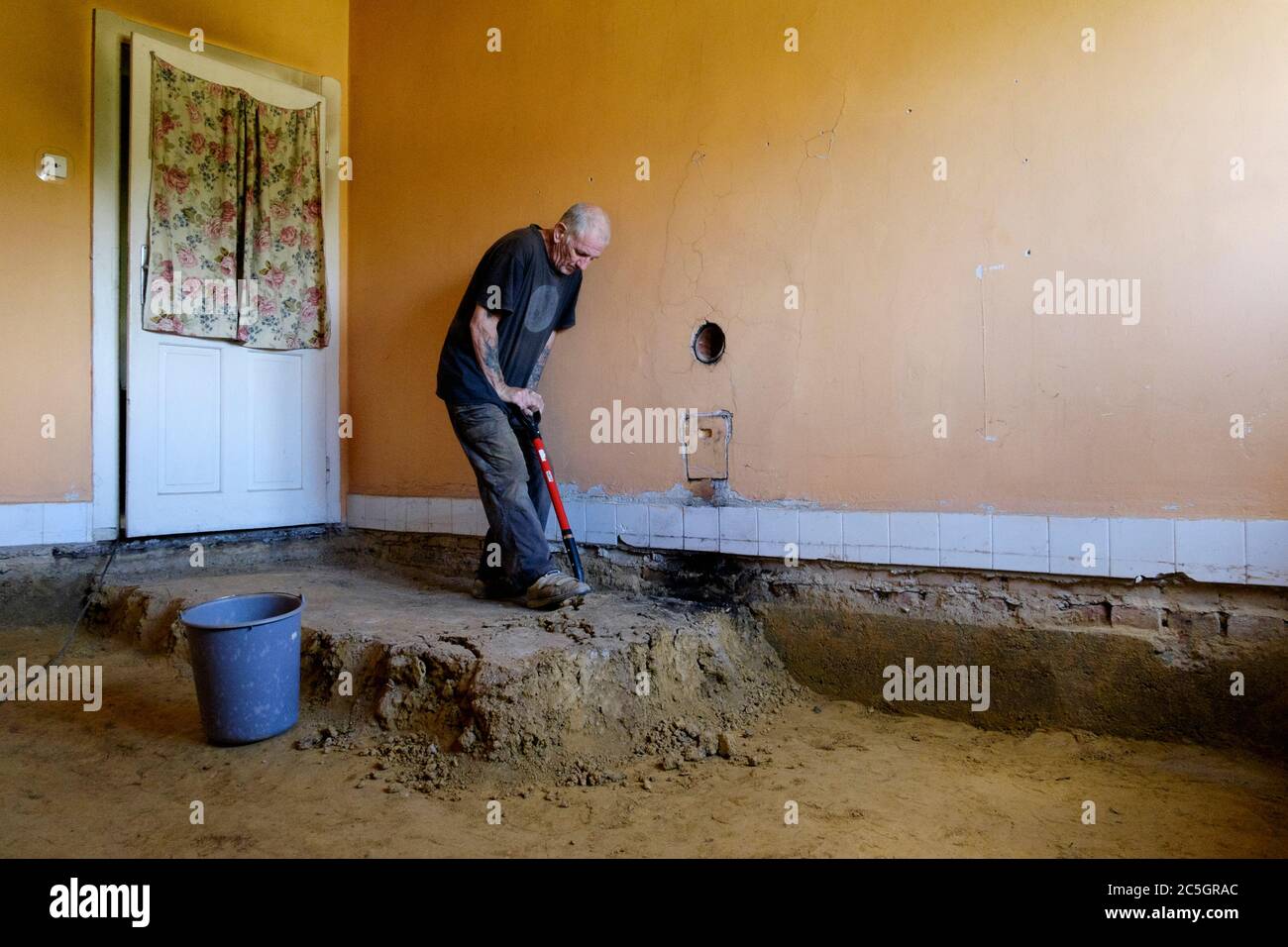 man using spade to dig up mud floor foundations during house ...