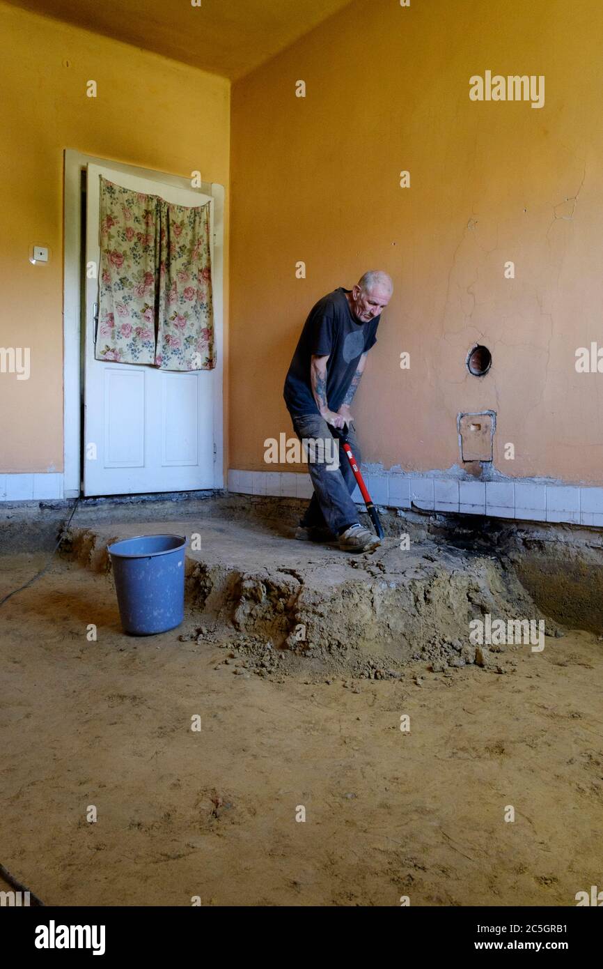 man using spade to dig up mud floor foundations during house ...