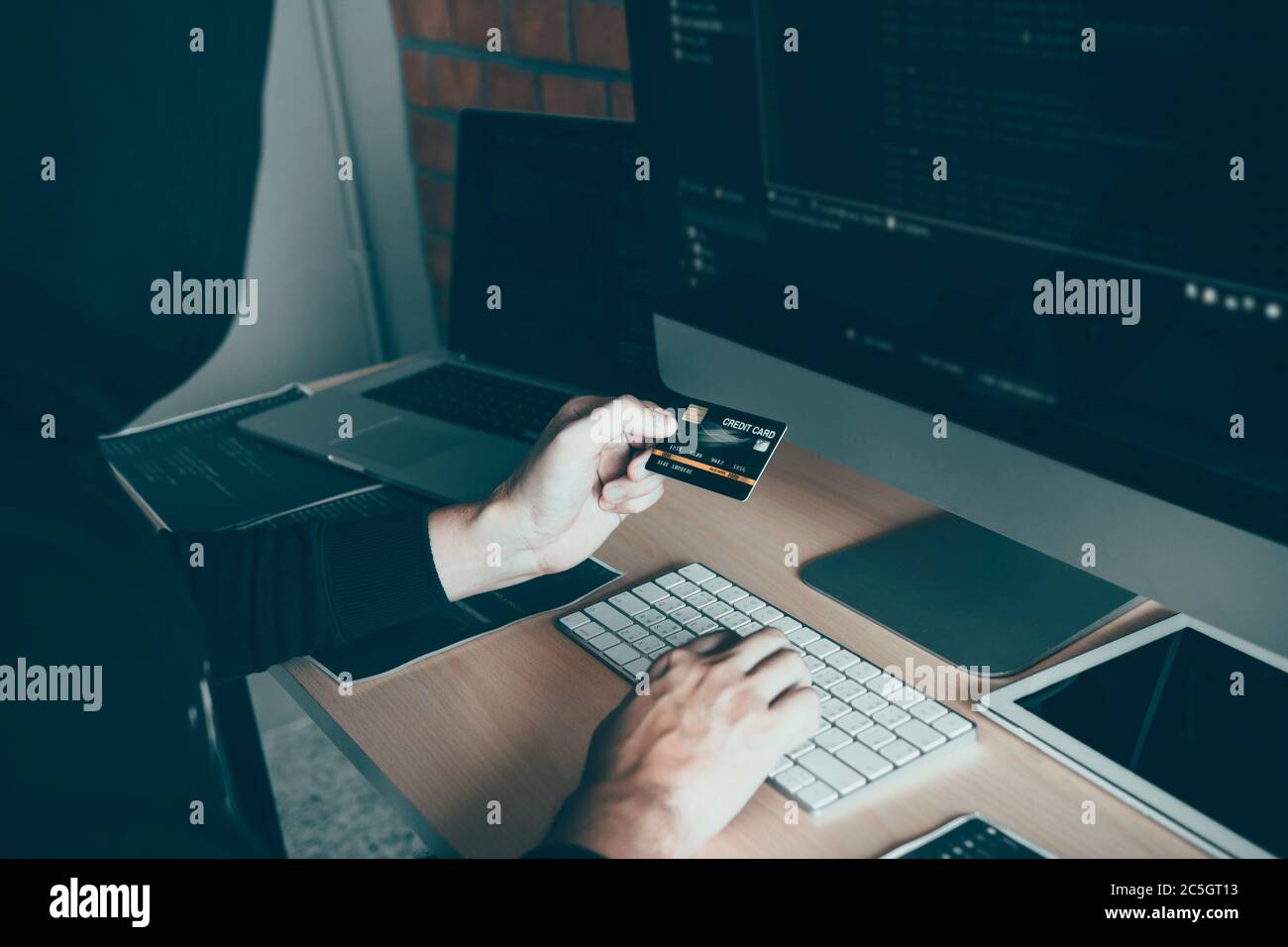Hacker in the hood working with computer and holding credit card with ...