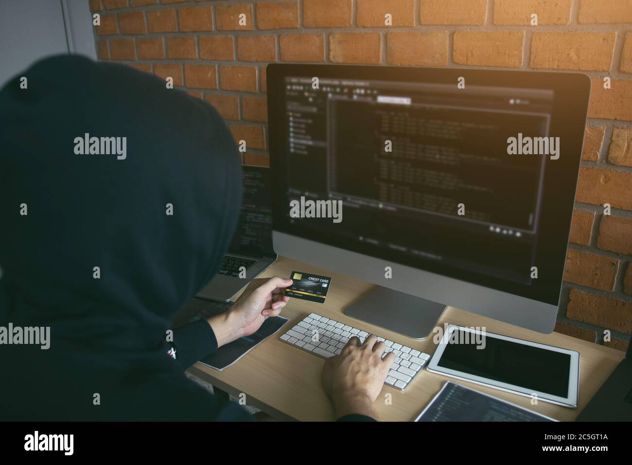 Hacker in the hood working with computer and holding credit card with ...