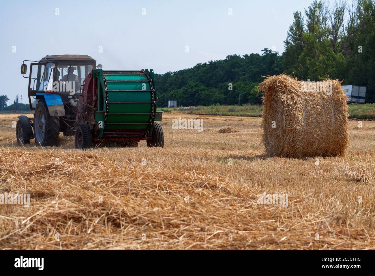 A tractor with a trailed bale making machine collects straw rolls in ...