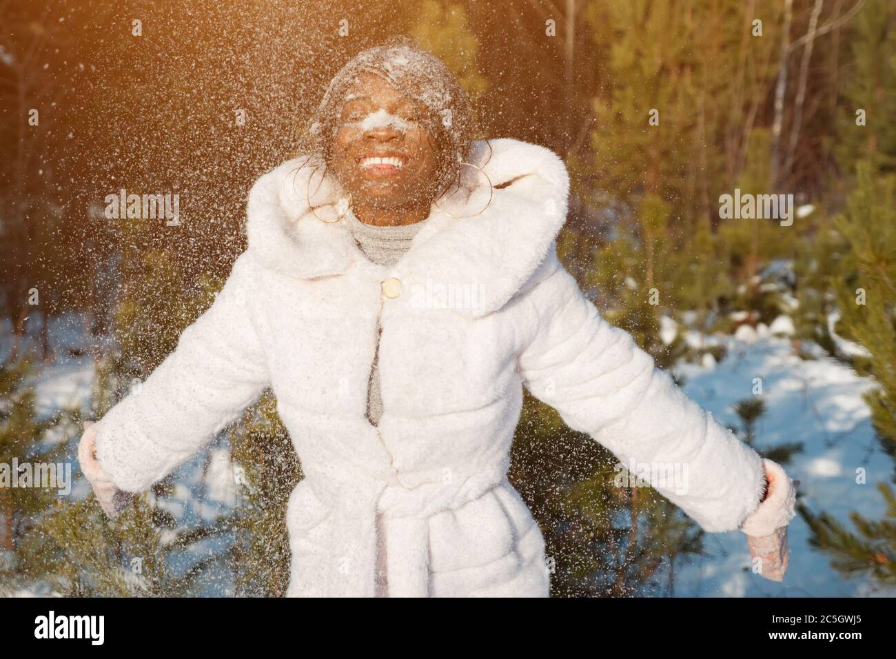 dark-skinned woman playing with snow hits her face and laughs sunlight ...