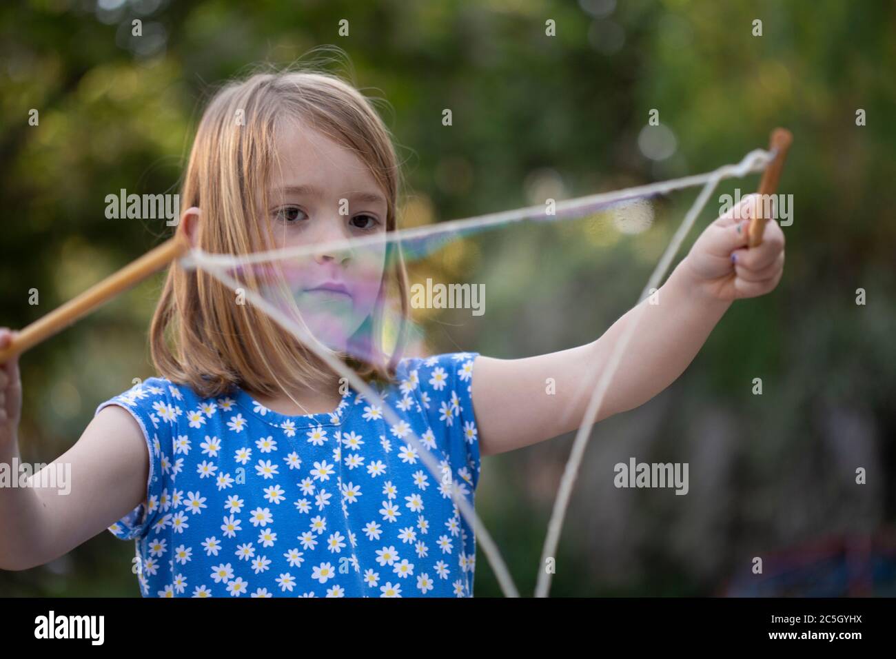Young girl in a blue and white dress blowing large bubbles with string ...
