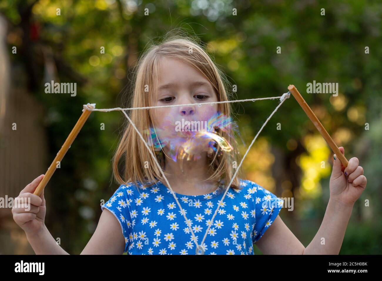 Young girl in a blue and white dress blowing large bubbles with string ...