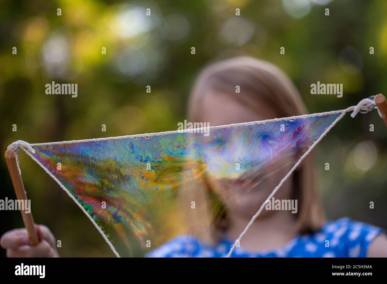 Young girl in a blue and white dress blowing large bubbles with string ...