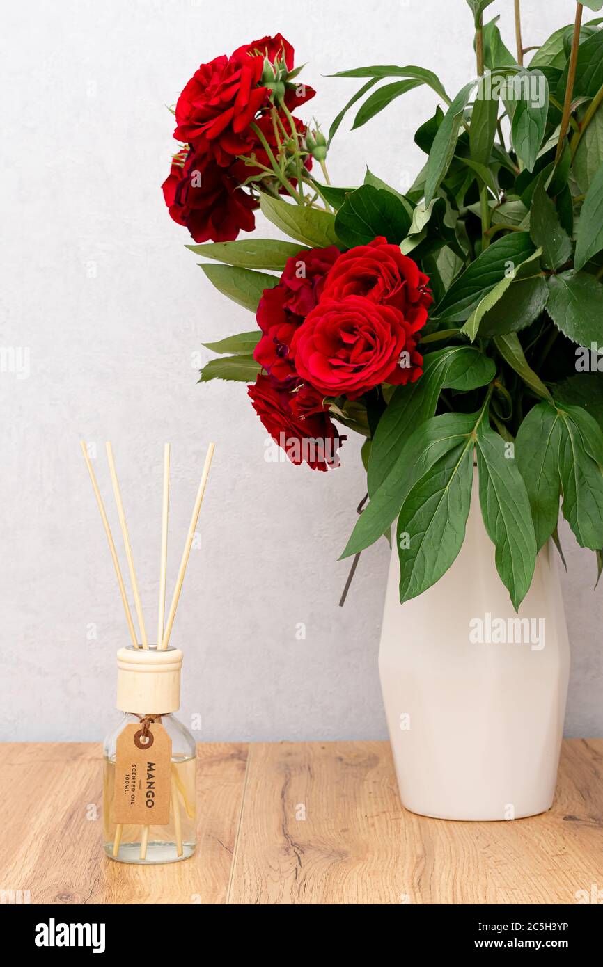 Aroma reed diffuser in the interior. Red rose flowers in vase on wooden ...