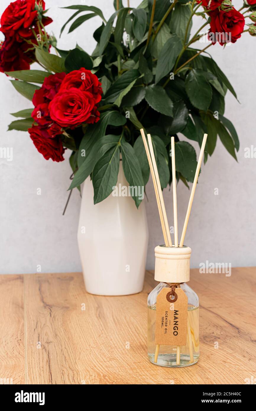 Aroma reed diffuser in the interior. Red rose flowers in vase on wooden ...