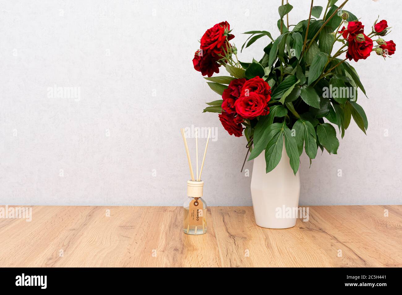 Aroma reed diffuser in the interior. Red rose flowers in vase on wooden ...