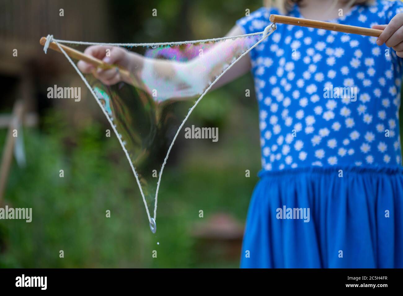 Young girl in a blue and white dress blowing large bubbles with string ...