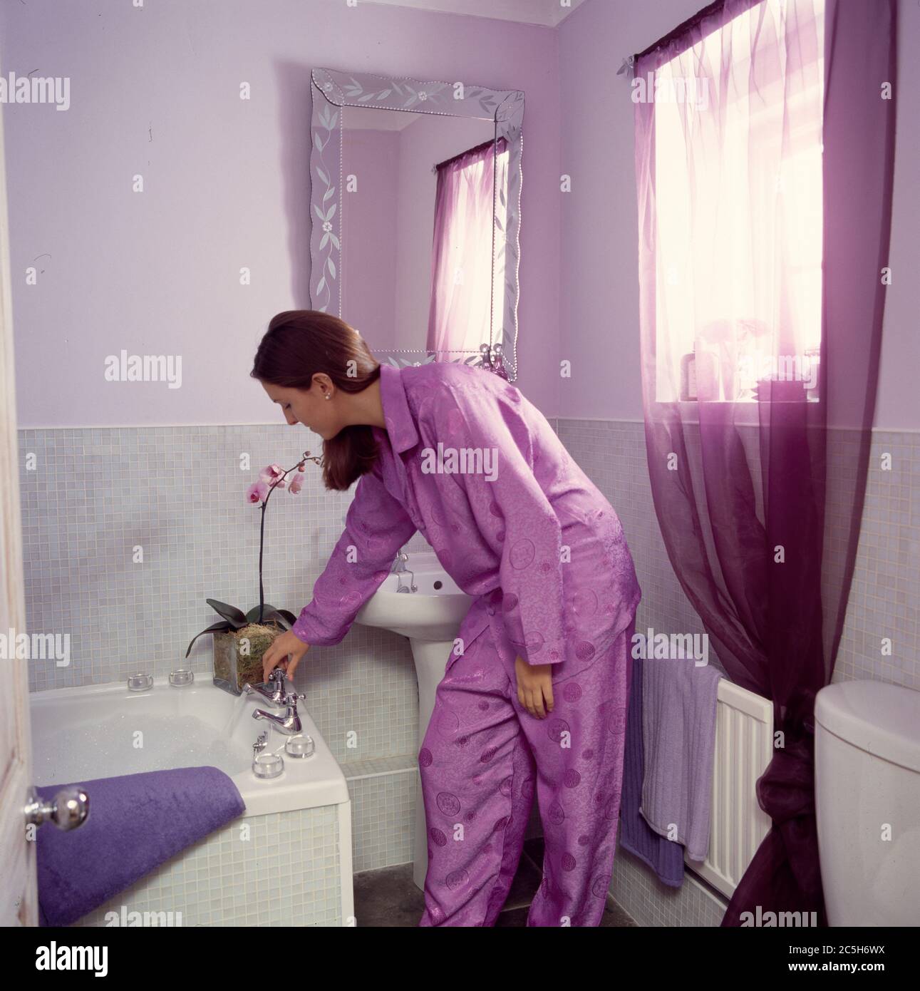 Woman in satin pyjamas turning on bath taps Editorial use only Stock ...