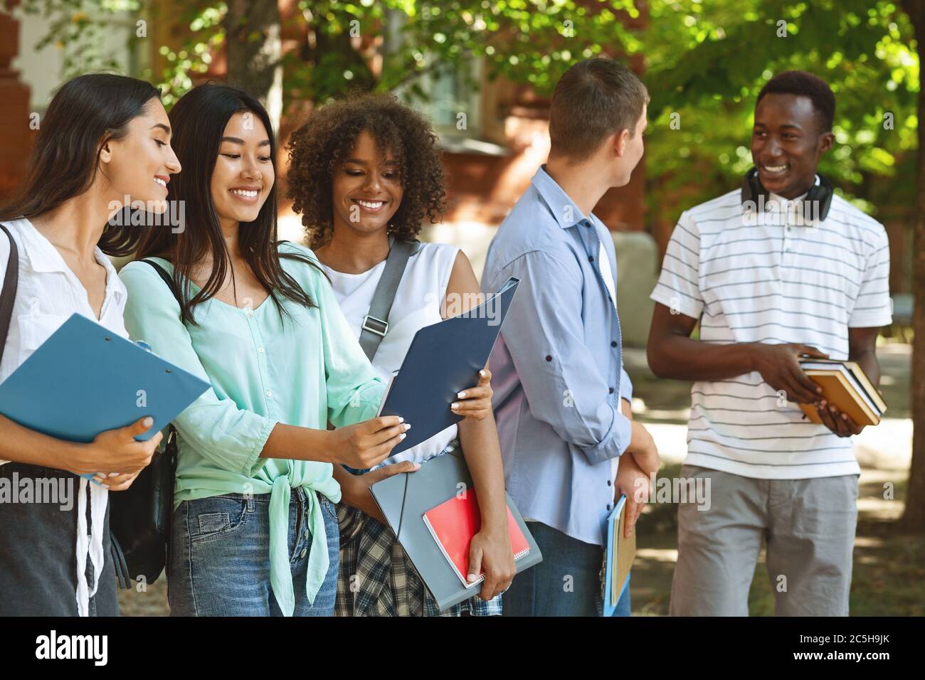 Portrait Of Smiling Students Standing Outdoors At Campus Courtyard ...