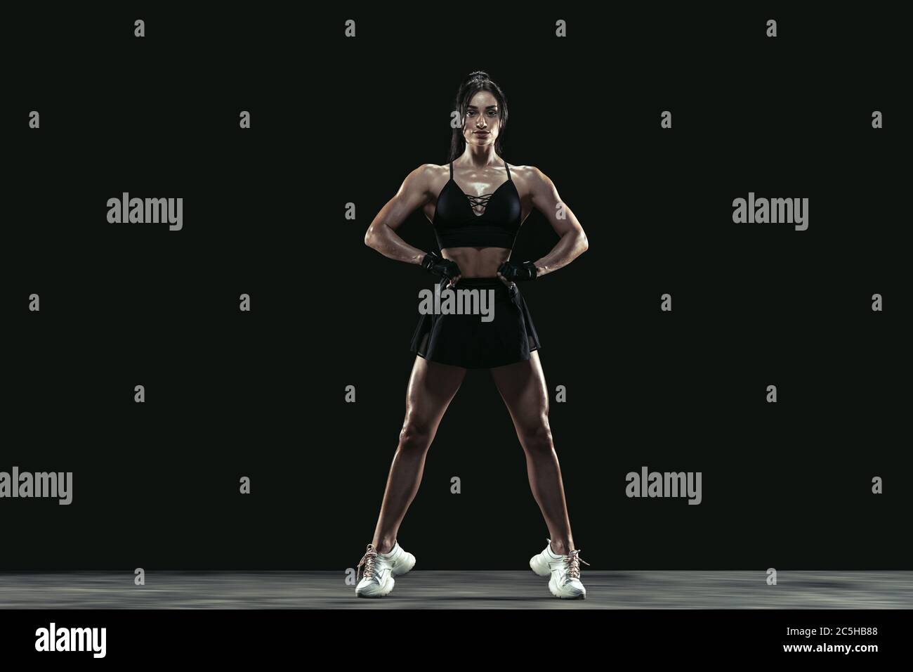 Beautiful young female athlete practicing on black studio background ...