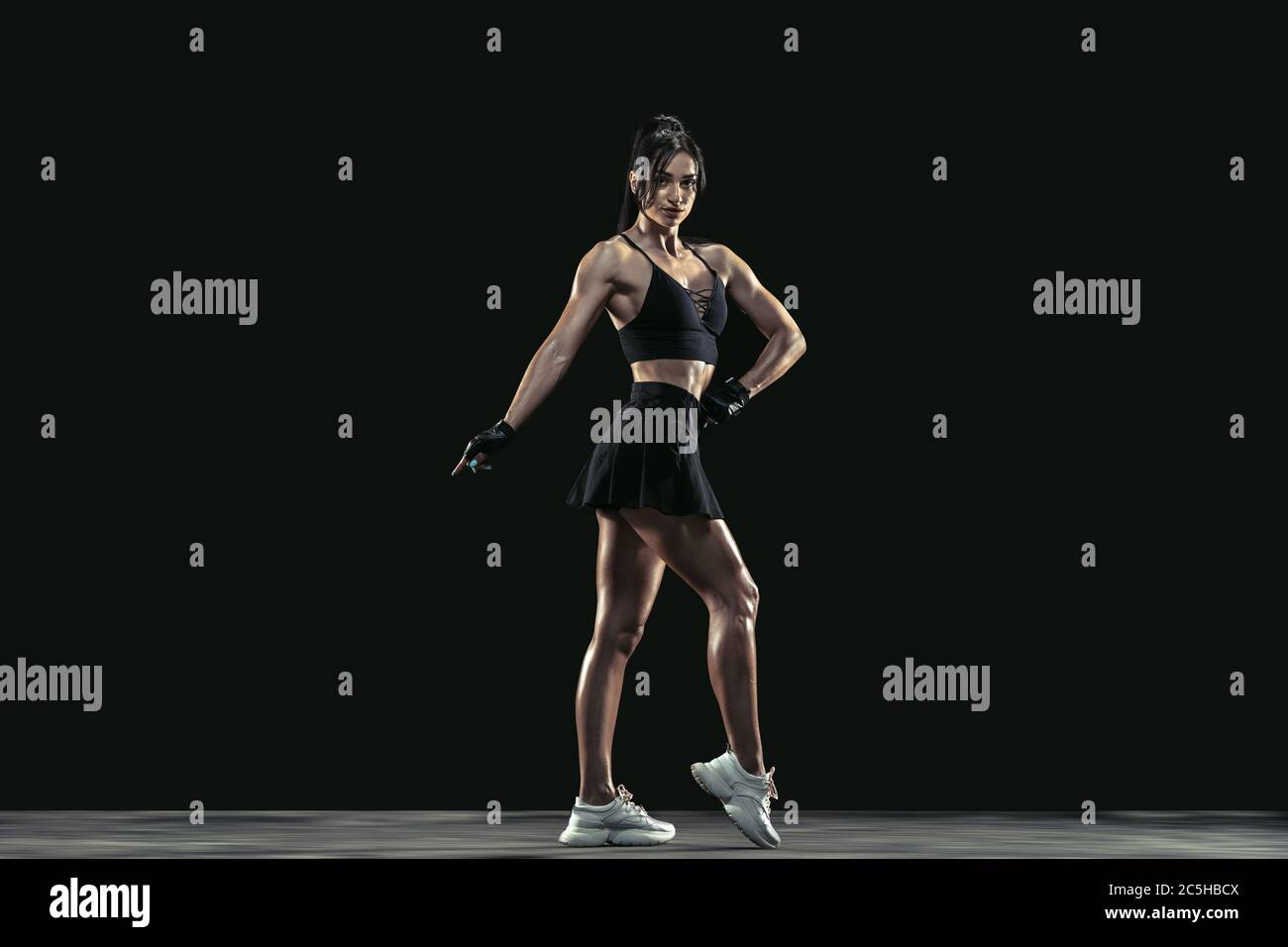 Beautiful young female athlete practicing on black studio background ...