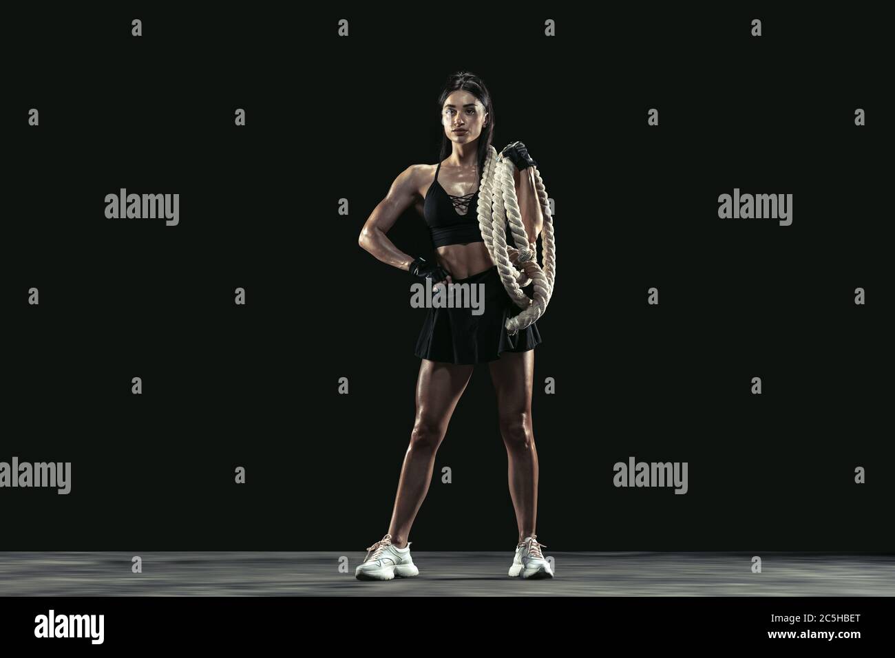 Beautiful young female athlete practicing on black studio background ...