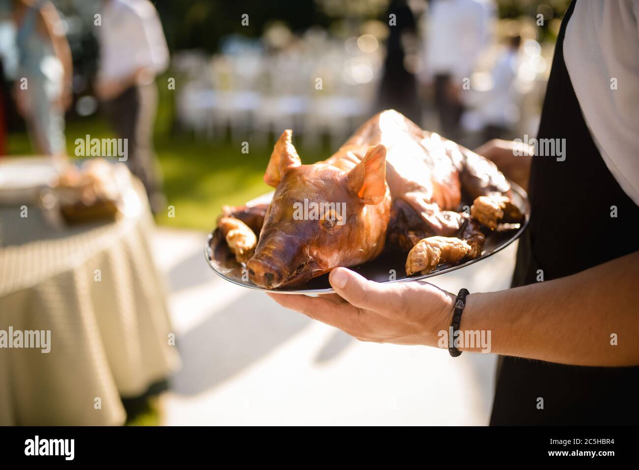 The waiter serves the roast pig on an oval at an outdoor party Stock ...