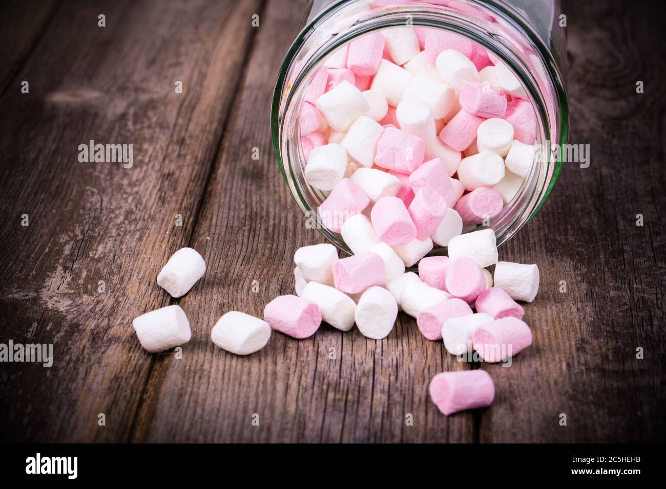 Pink and white marshmallows spilling from a storage jar, over old wood ...