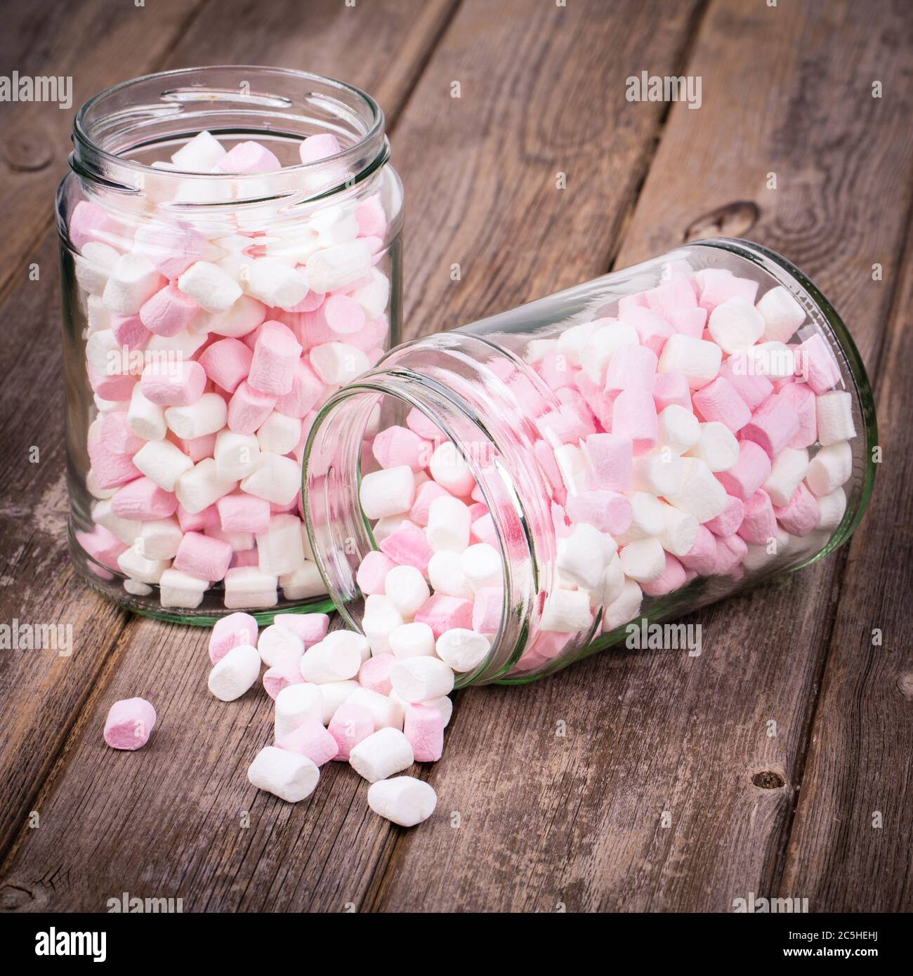 Pink and white marshmallows spilling from a storage jar, over old wood ...