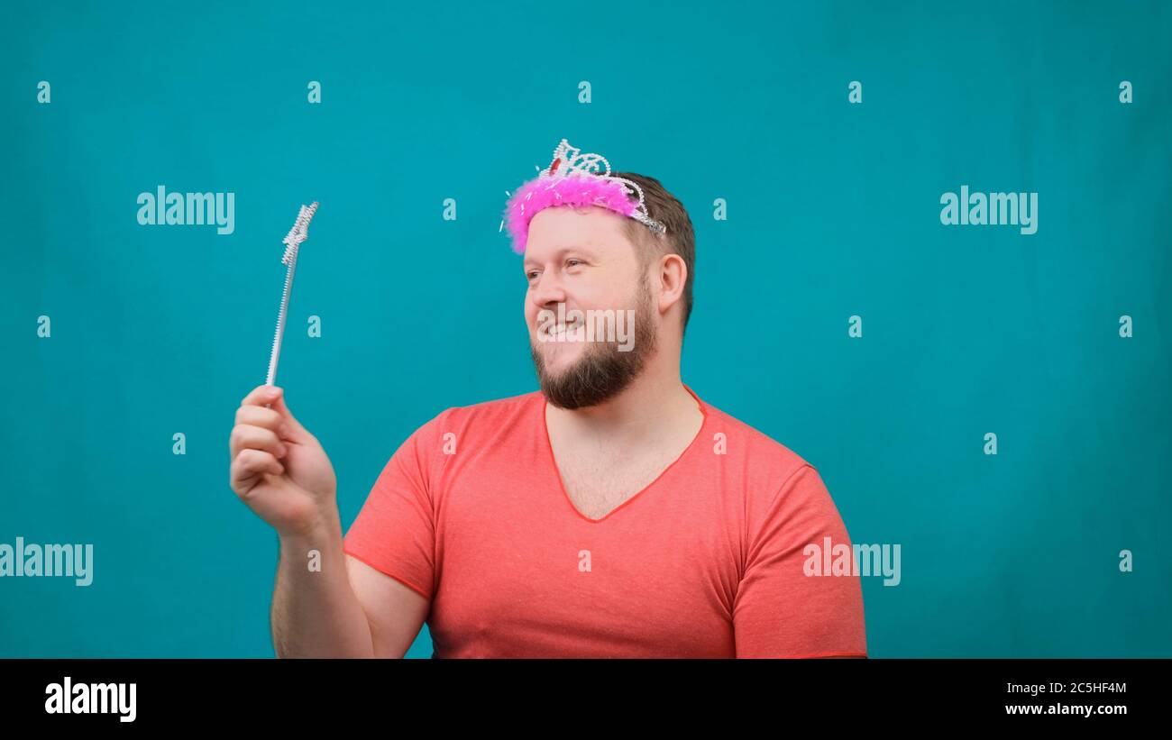 Cute bearded freaky man in a pink T-shirt with a deadema on his head ...