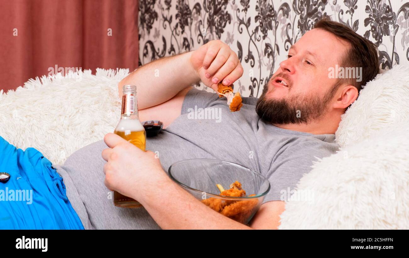fat man drinks beer and eats unhealthy food chicken wings, bored in ...