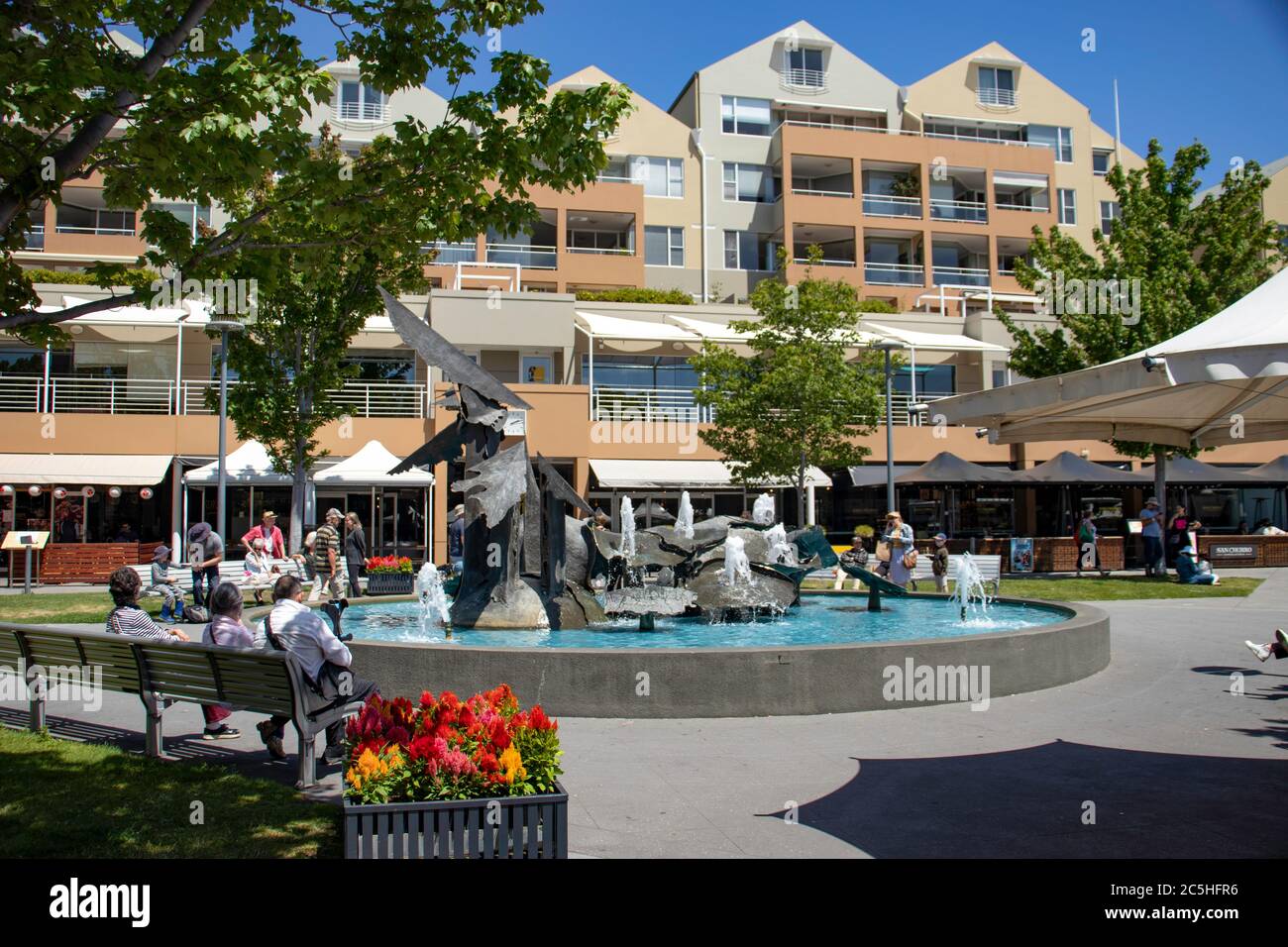 Fountain in a town square surrounded by tourists and colorful plants ...