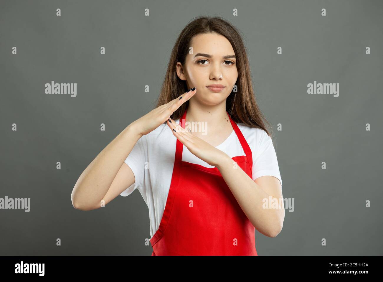 Portrait of female supermarket employee making time out gesture on gray ...