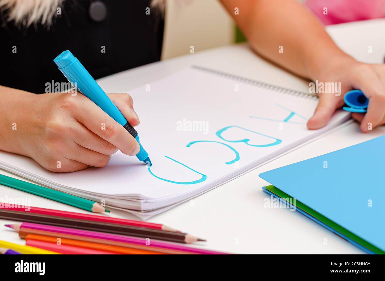 Hands of a child writing letters with blue marker on white. English ...