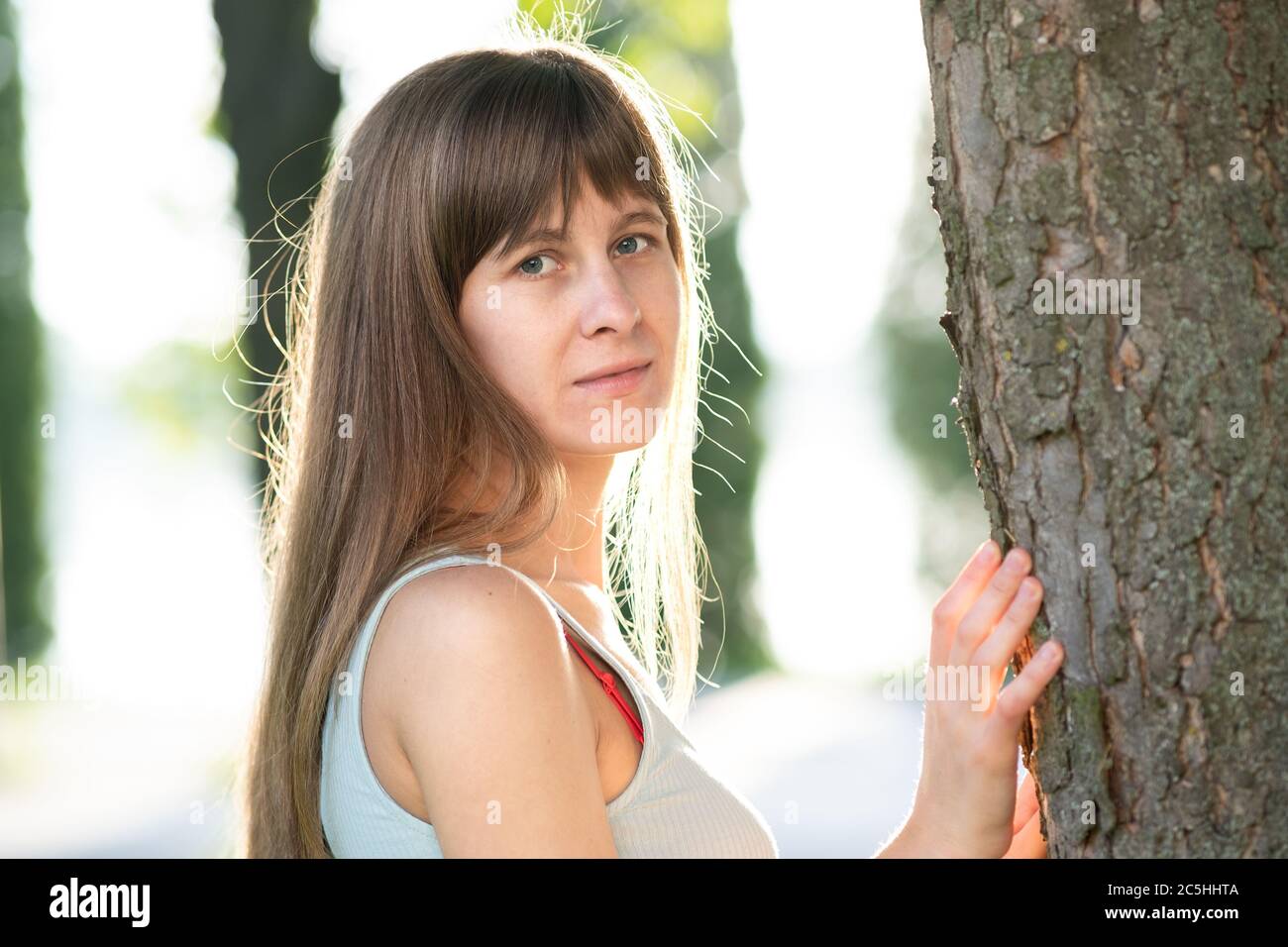 Portrait of pretty young woman standing neat tree trunk in summer Stock ...