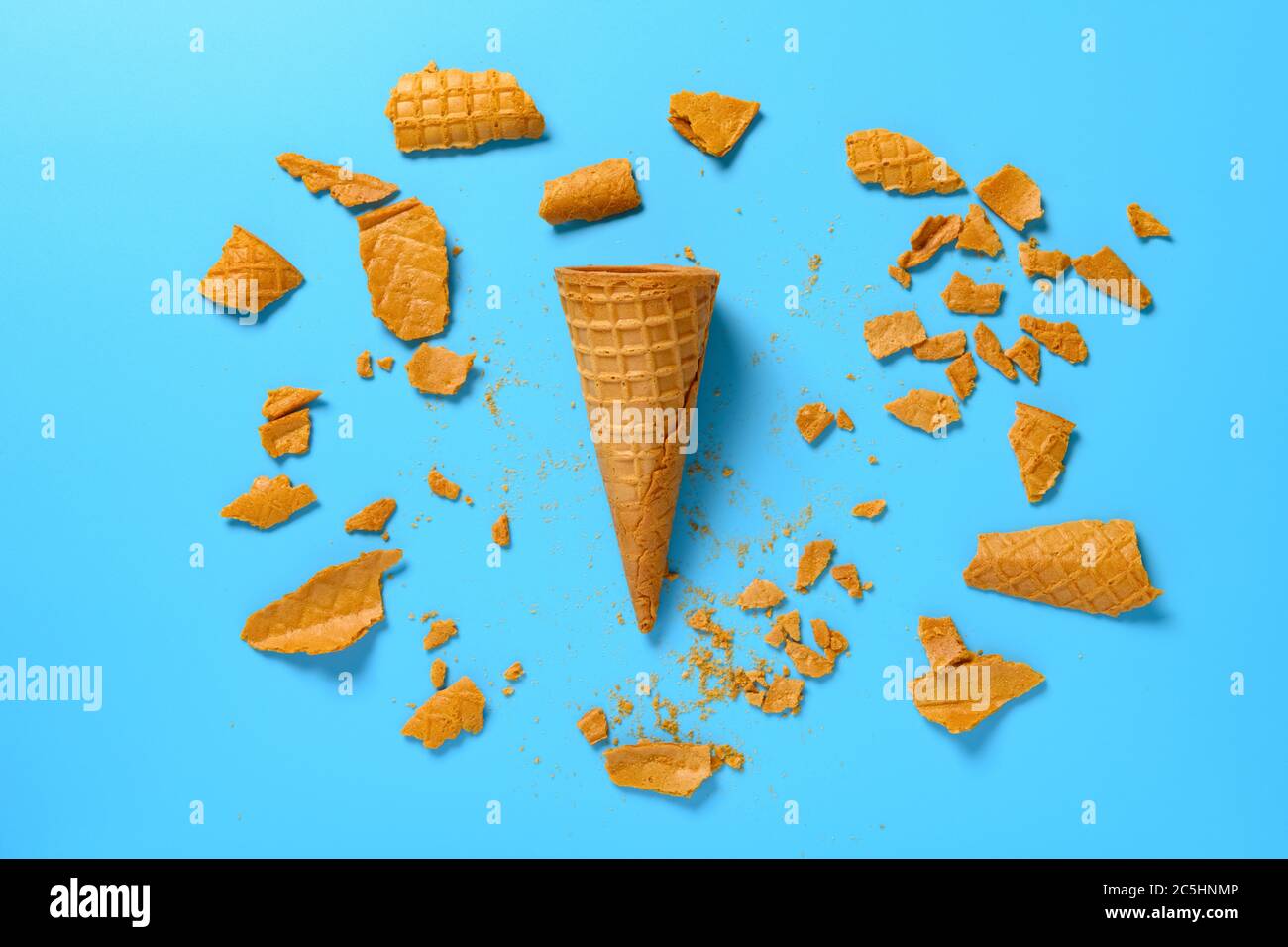 an intact ice cream cone surrounded by broken fragments on blue ...
