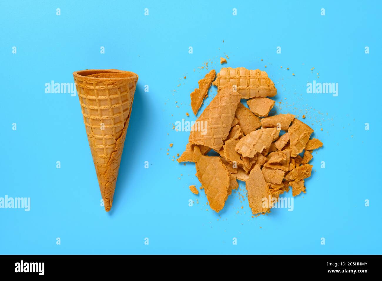 an intact ice cream cone with a broken one nearby on blue background ...