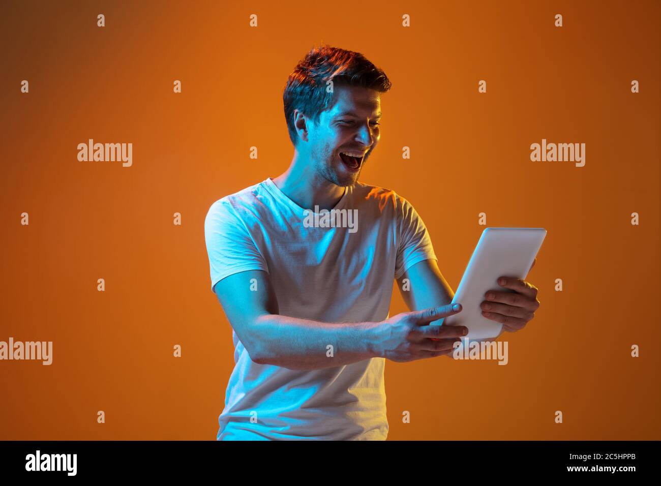 Laughting scrolling tablet. Caucasian young man's portrait on gradient ...
