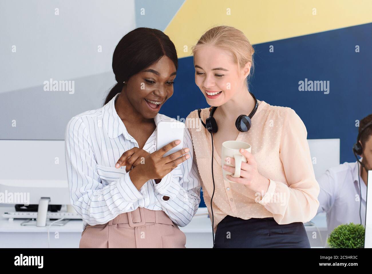 Female call centre operators watching video on smartphone during coffee ...