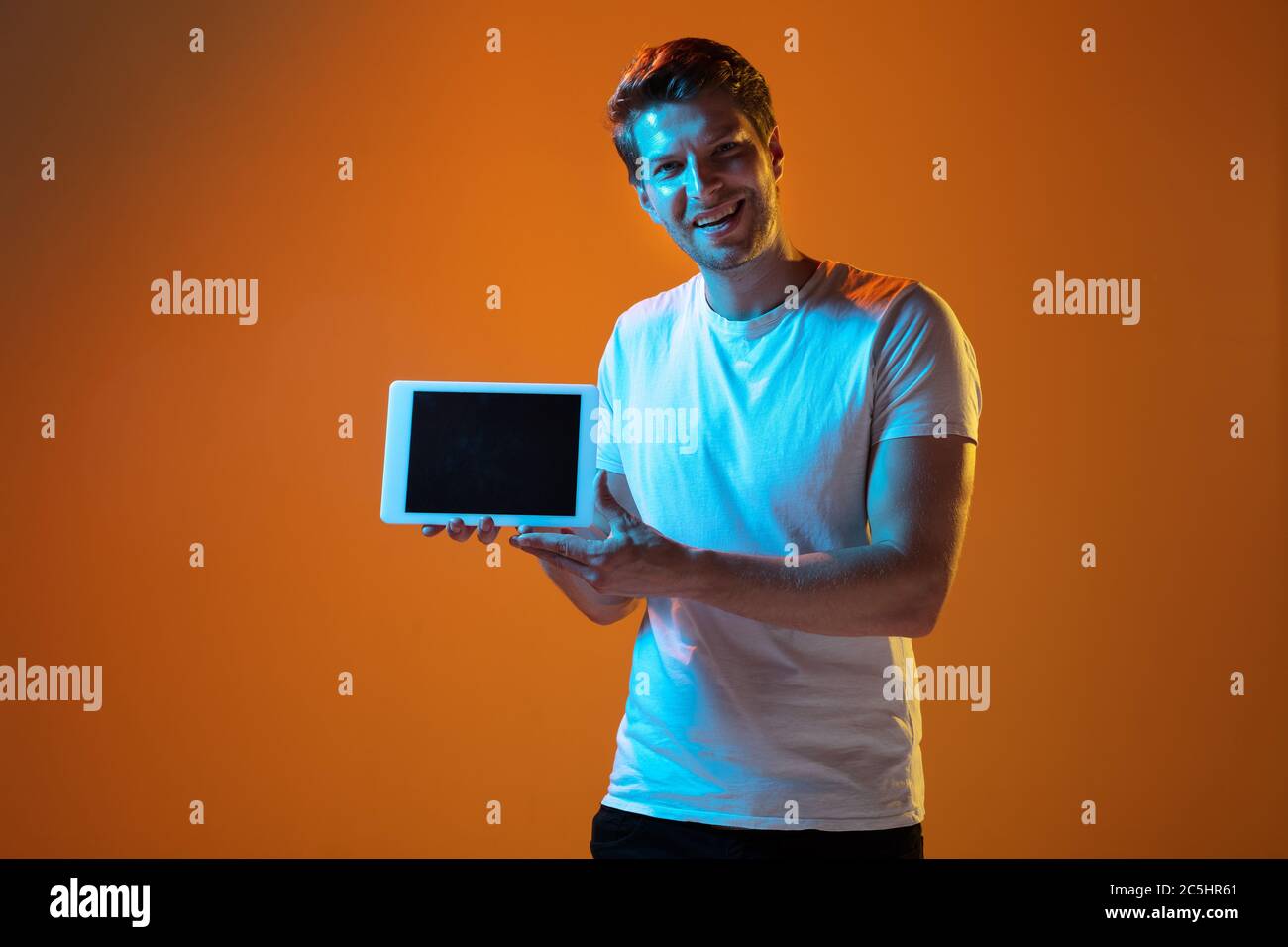 Smiling, showing tablet. Caucasian young man's portrait on gradient ...