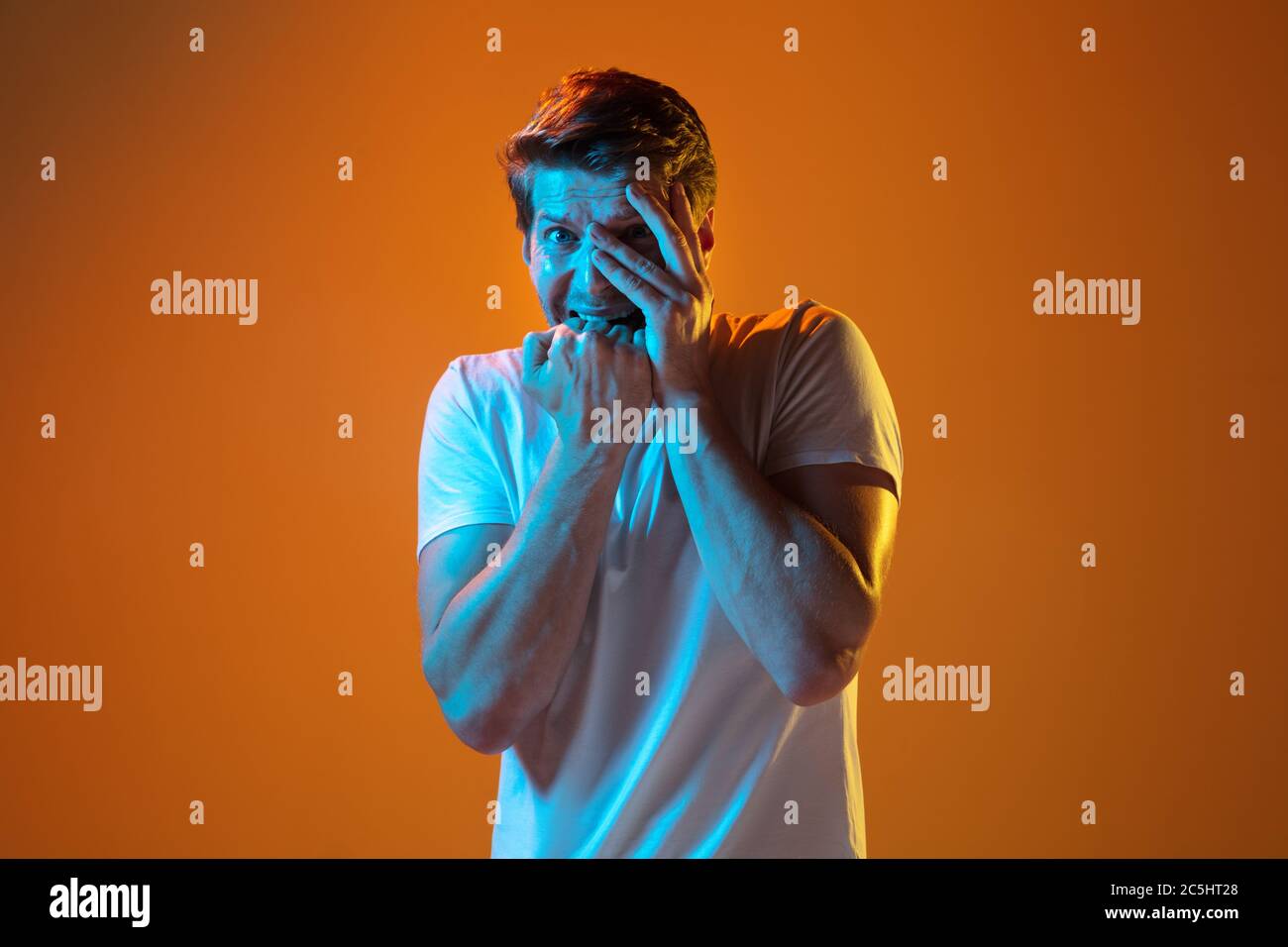 Scared hiding face. Caucasian young man's portrait on gradient orange ...