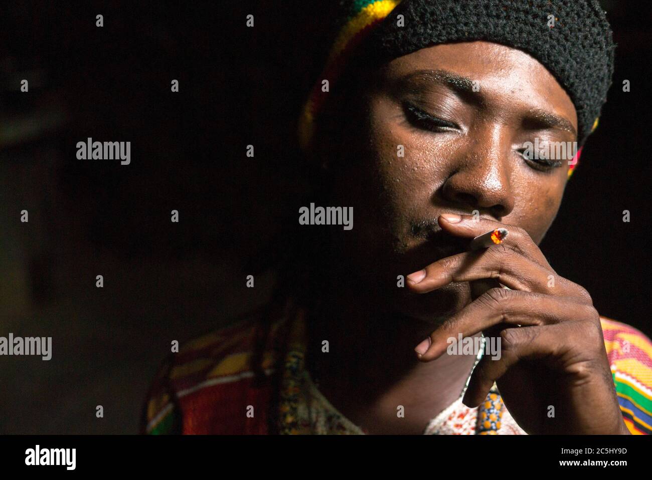 Face of young handsome African Rastafarian man smoking outdoors at ...
