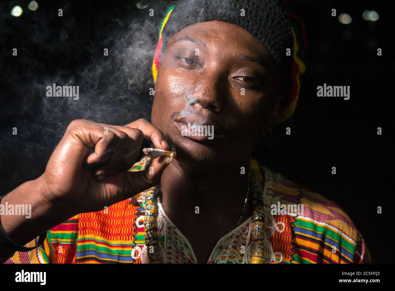 Face of young handsome African Rastafarian man smoking outdoors at ...