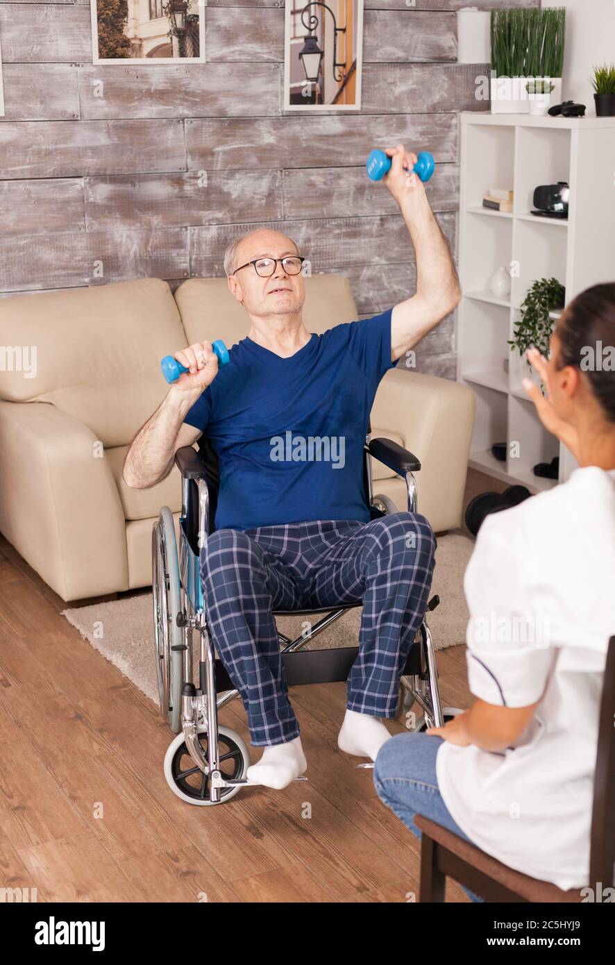 Invalid senior man in wheelchair training with dumbbells during ...