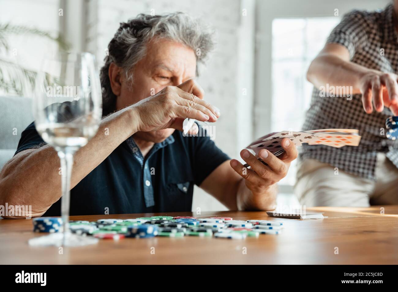 Shuffling. Two happy mature friends playing cards and drinking wine ...