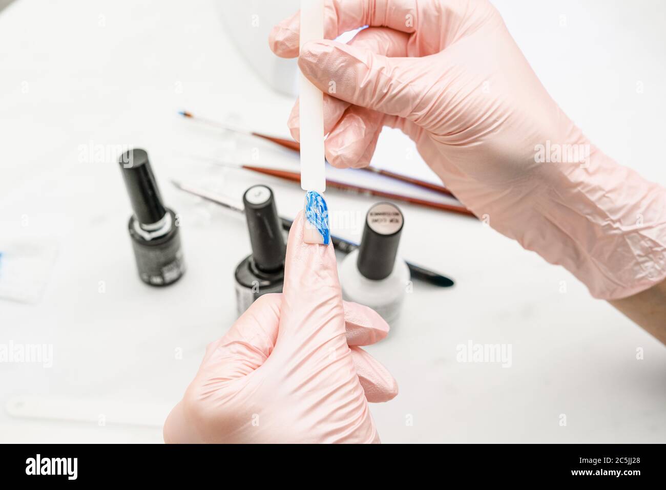 Manicurist at work in the office. Drawing gel polish on tips, creating ...