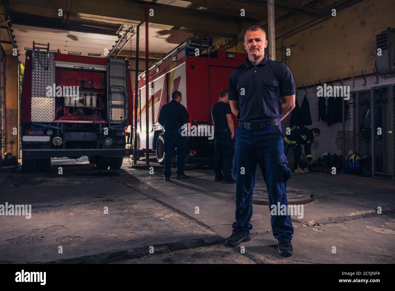 Portrait of handsome firefighter standing against trucks at fire ...