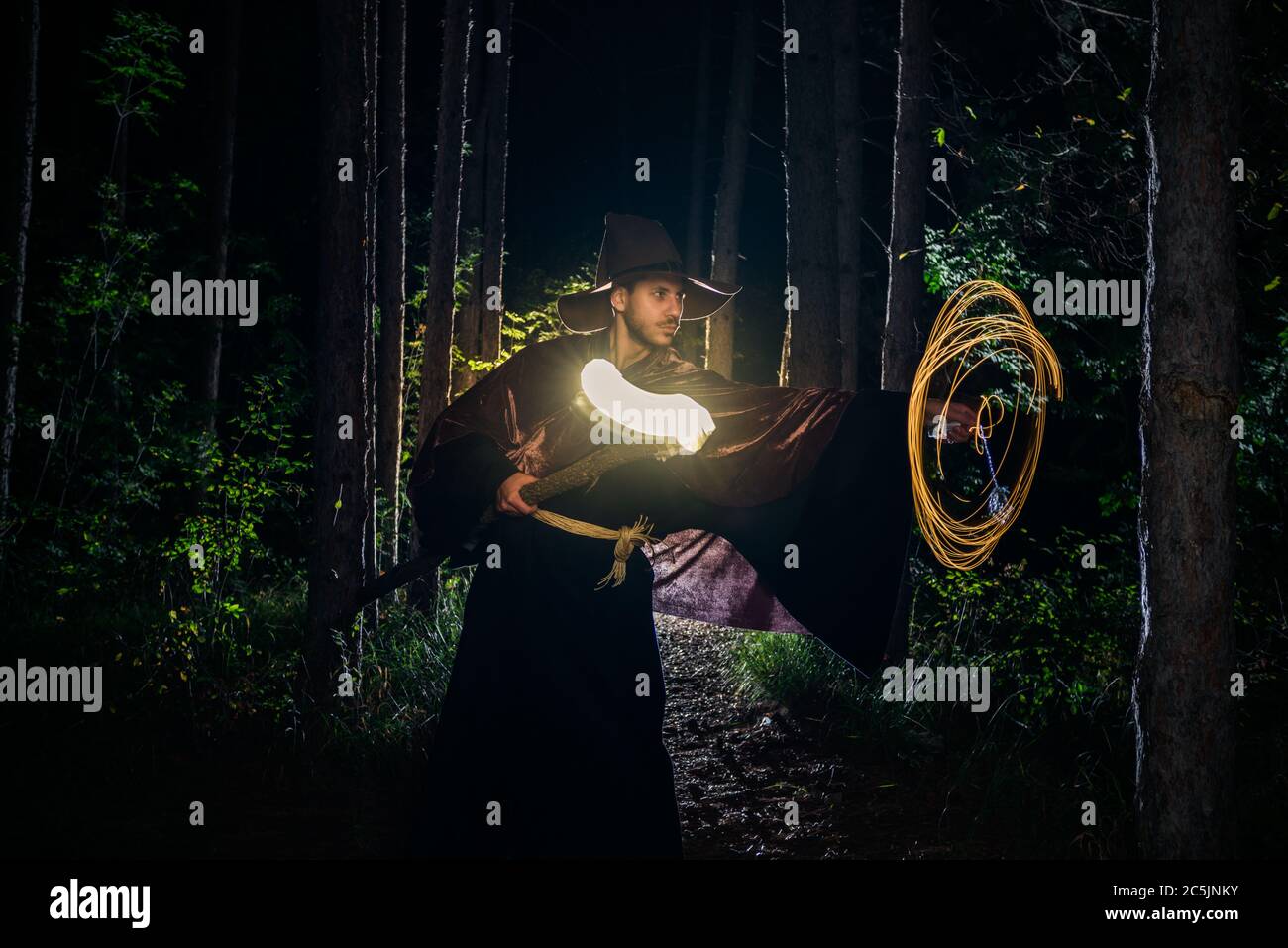 Wizard costume wearing guy with wooden staff standing between trees for ...