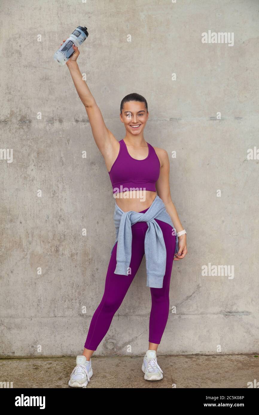 Woman wearing leggings and sports bra with one arm raised in the air ...