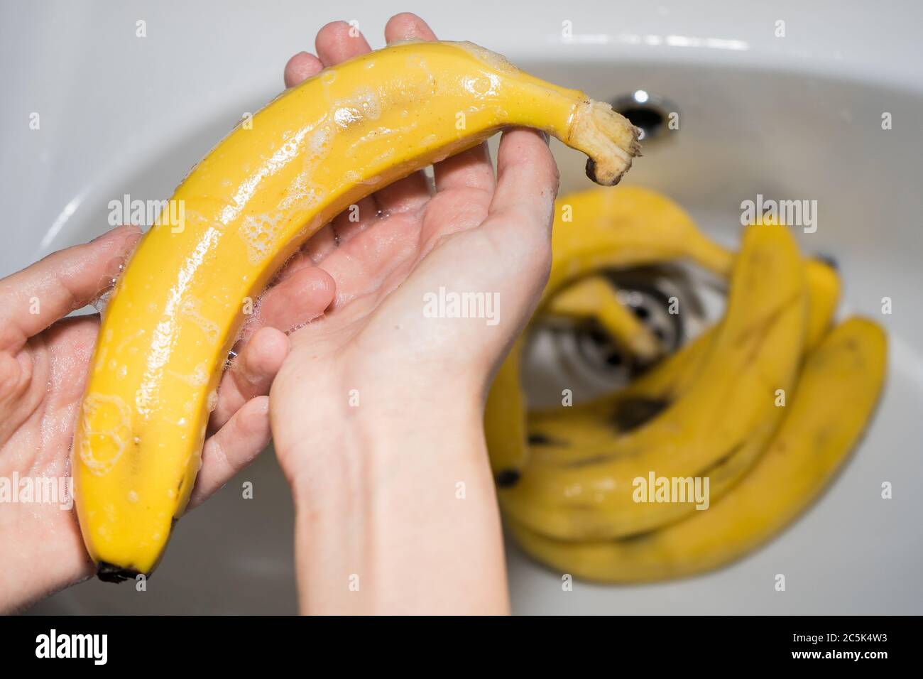 Girl washes bananas with soap. Hands and soapy bananas in the sink ...