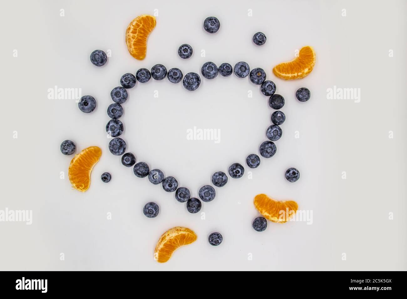 A heart's frame from mandarin pieces and blueberry on white background ...