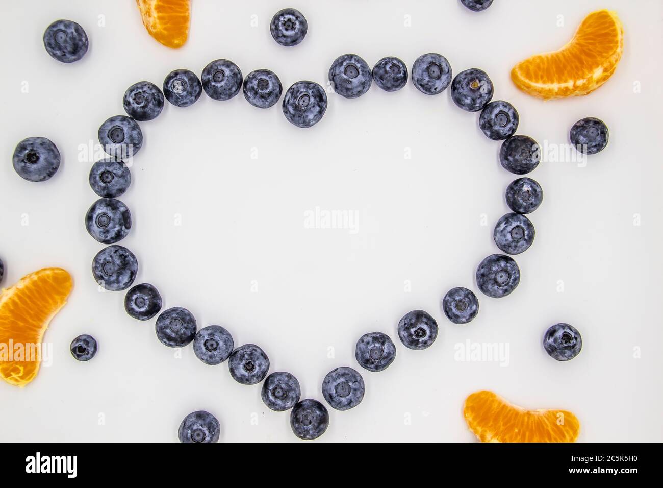 A heart's frame from mandarin pieces and blueberry on white background ...