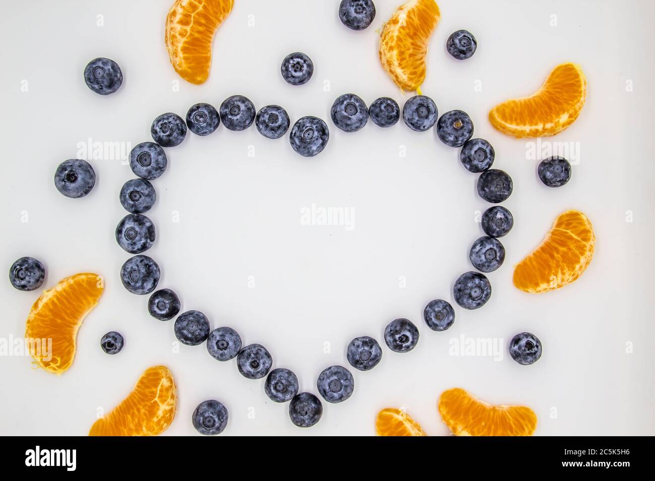 A heart's frame from mandarin pieces and blueberry on white background ...