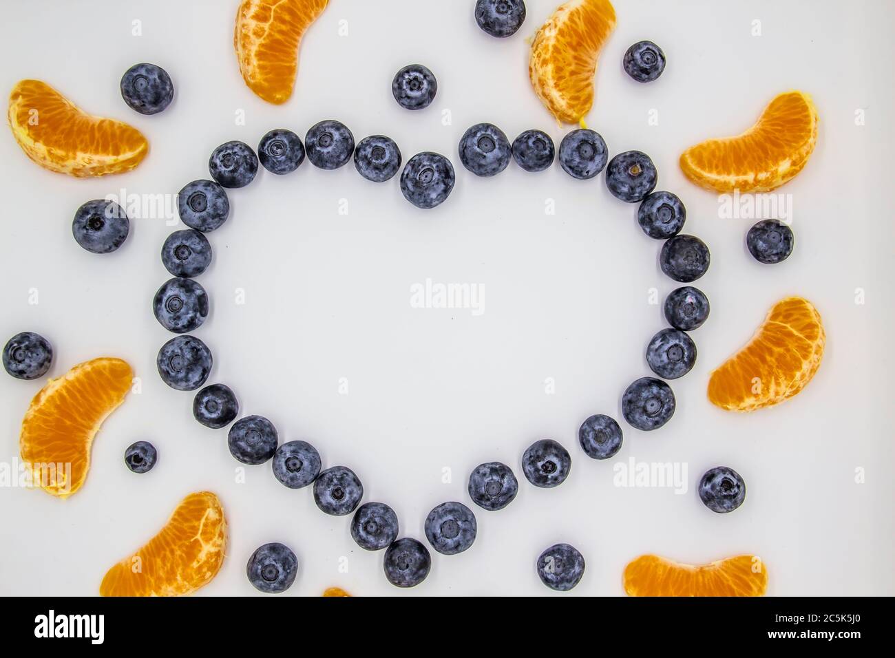 A heart's frame from mandarin pieces and blueberry on white background ...